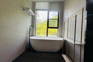 Uma casa de banho moderna com uma banheira independente, uma janela com vista para uma paisagem verde e um porta-toalhas.