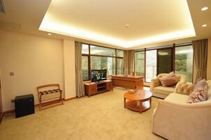 Uma sala de estar ampla com sofá, mesa de centro, TV e grandes janelas com vista para o exterior.