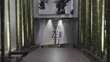 Um corredor com estruturas verticais semelhantes a bambu, uma placa na parede com a inscrição "HOTEL WITH ZEN TIM-ES RESORT" e um piso com padrão claro.