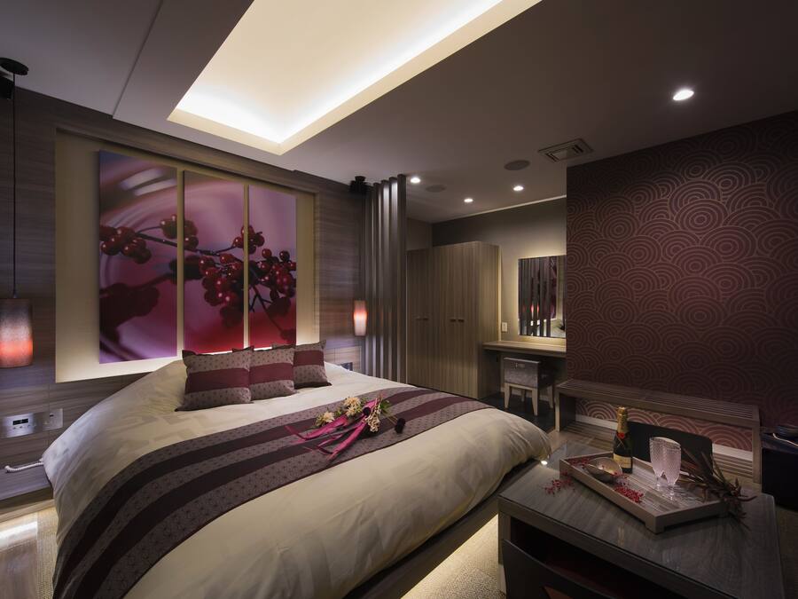 Quarto de hotel moderno com cama grande, mesas de cabeceira, criado-mudo, escrivaninha e espelho.