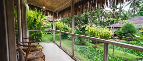 Varanda com vista para um jardim exuberante e uma construção com telhado de palha.