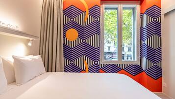 Quarto de hotel com cama, cortinas, janela e vista, e parede com padrão geométrico.