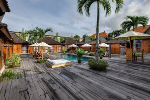 Um deck de madeira com piscina, cabanas de madeira e palmeiras.