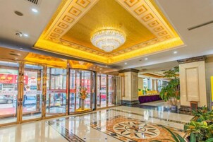 Um saguão de hotel com um lustre imponente, piso de mármore e entrada por porta de vidro.