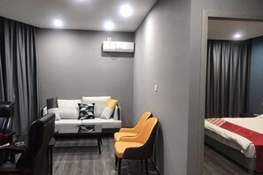 Quarto de hotel moderno com sofá, duas cadeiras, escrivaninha e cama.