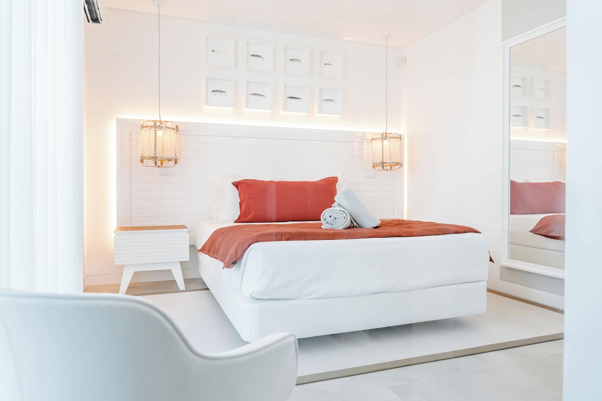 Quarto moderno com cama, mesas de cabeceira, uma cadeira e um espelho grande.