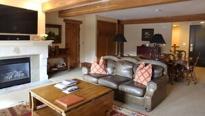 Uma sala de estar aconchegante com lareira, sofá de couro, mesa de centro de madeira e televisão.