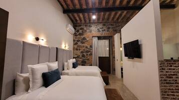 Quarto de hotel com duas camas, parede de pedra, teto de madeira e televisão fixada na parede.