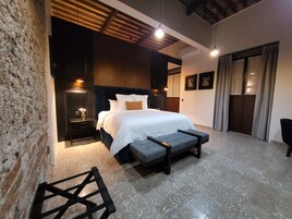 Quarto moderno com uma cama grande, mesas de cabeceira, um banco e uma parede de pedra.