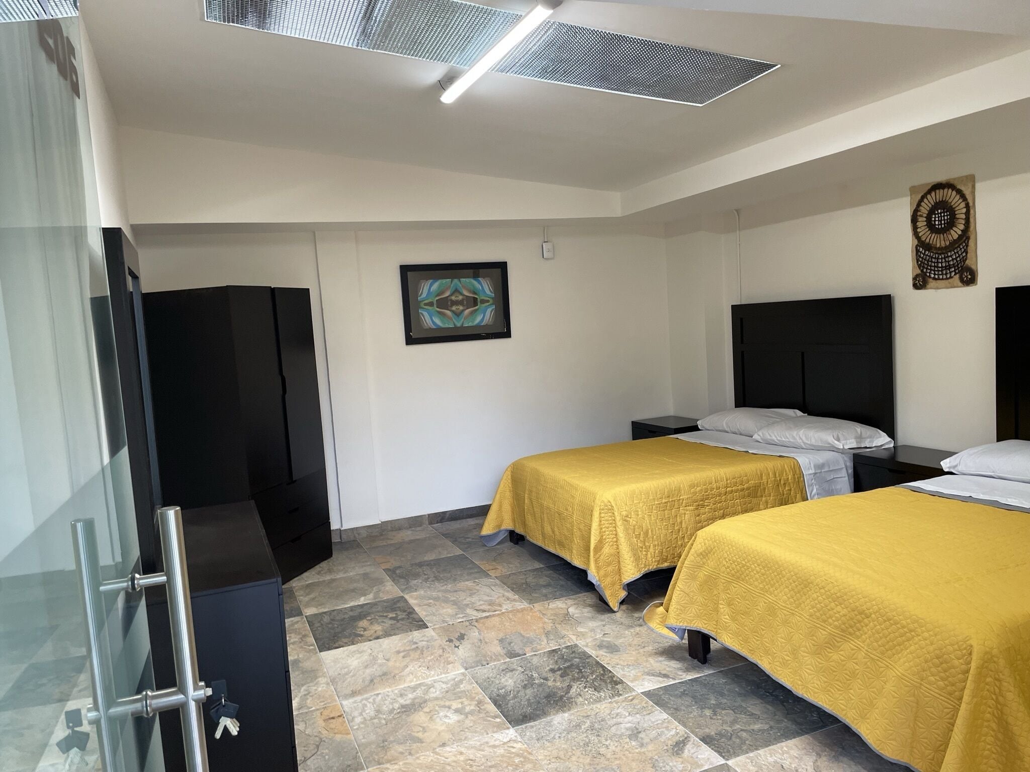 Quarto de hotel com duas camas, televisão, guarda-roupa e um quadro na parede.