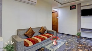 Um saguão de hotel com um sofá, uma mesa de centro de vidro, um ar condicionado, uma porta de madeira e um visor digital.