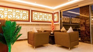 Um hall com dois sofás, um balcão de recepção, painéis decorativos e uma janela ampla.