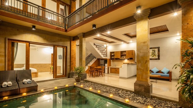 Uma área de piscina interior ampla, com um deck de madeira, espaço para sentar com almofadas, e uma escadaria que dá acesso a um andar superior.