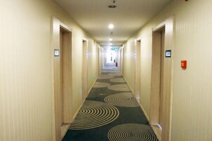 Corredor de hotel com portas em ambos os lados, um carpete estampado e placas de saída de emergência.