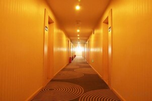 Corredor de hotel com portas em ambos os lados, carpete estampado e iluminação no teto.