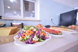 Uma mesa de buffet com diversos alimentos, incluindo saladas, frutas e pão.