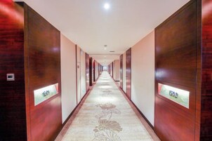 Corredor de hotel com lambris de madeira, portas de quartos numeradas e piso coberto de carpete.