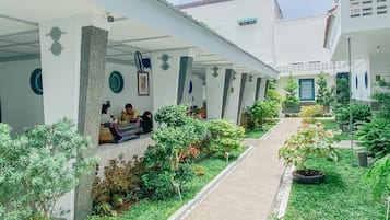 Um caminho lateralmente ladeado por áreas de estar cobertas, com vegetação e plantas em vasos.