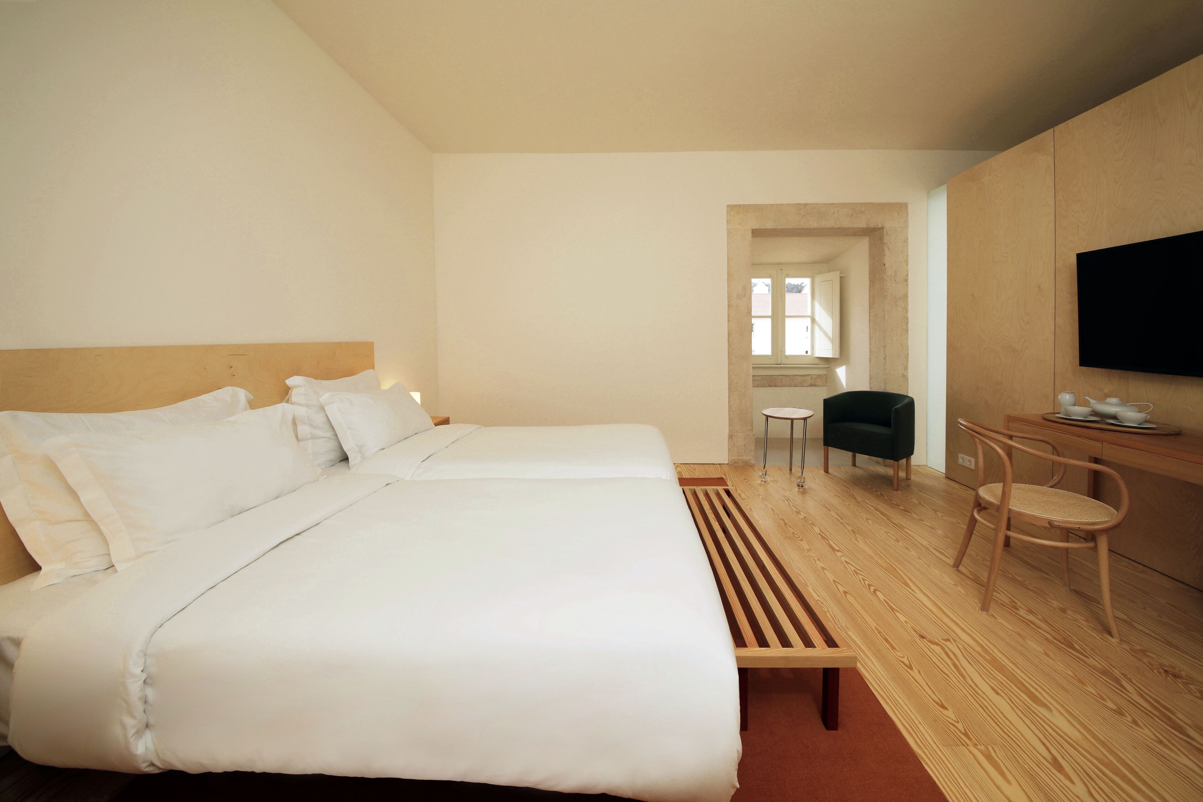 Quarto de hotel com uma cama grande, uma escrivaninha com cadeira, uma televisão e uma pequena mesa.