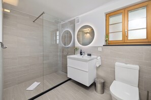 Um banheiro moderno com chuveiro de vidro, um espelho sobre o lavatório branco e um vaso sanitário.