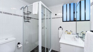 Um banheiro moderno com box de vidro, vaso sanitário branco, pia com produtos de higiene e espelho com padrão listrado.