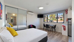 Quarto de hotel com cama, escrivaninha, cadeira, janela com vista e extintor de incêndio.