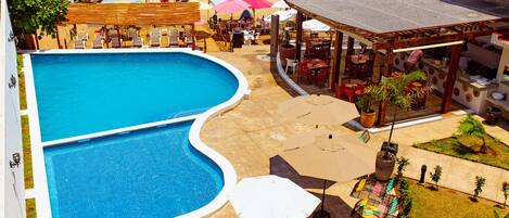 Área de piscina com piscina em curva, mobiliário de exterior, guarda-sóis e vista para a praia.