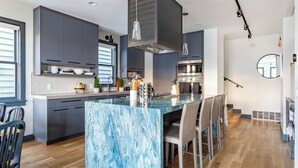 Uma cozinha moderna com armários cinza, uma ilha de mármore e eletrodomésticos de aço inoxidável.