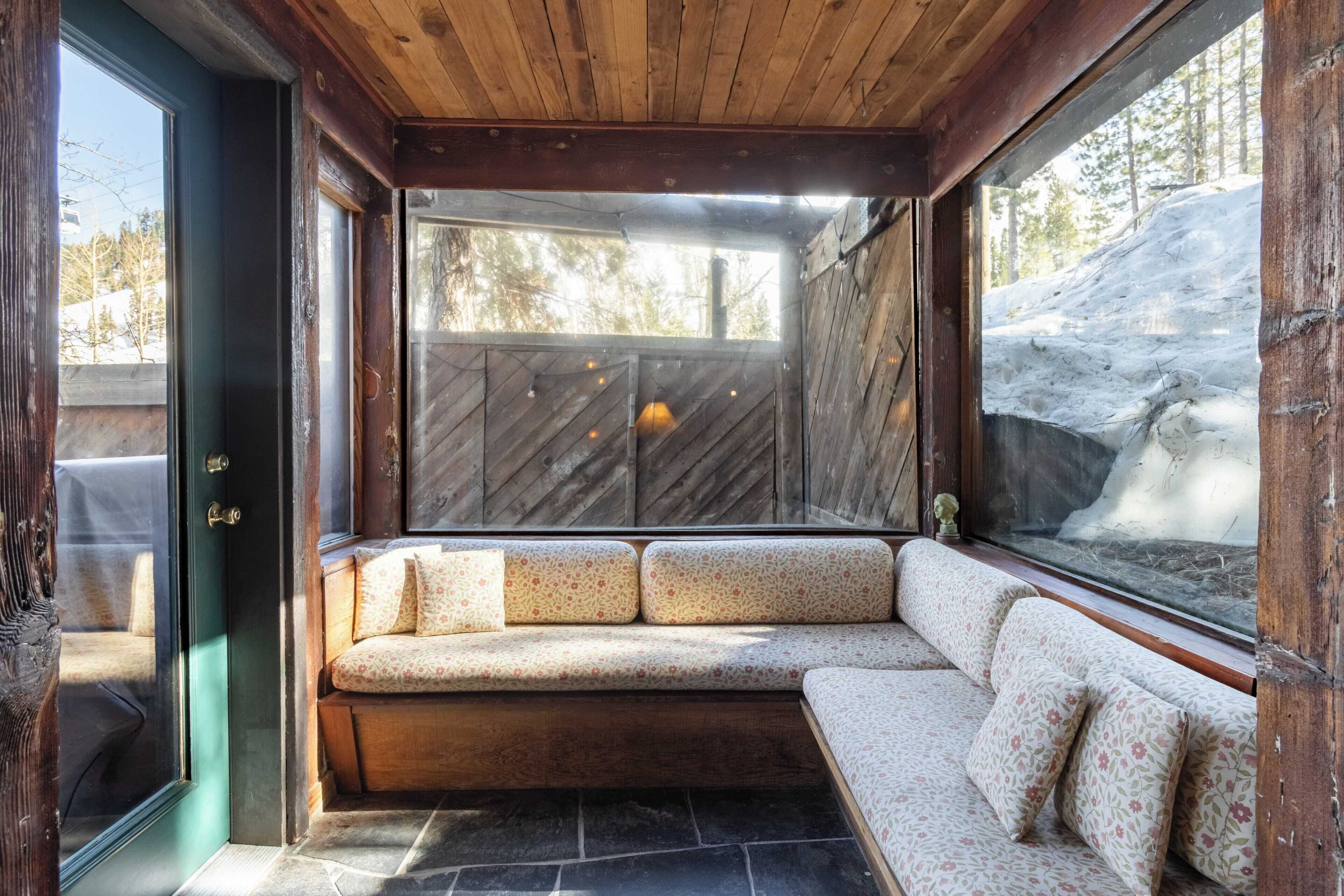 Interior de uma cabana de madeira com um banco embutido e uma grande janela com vista para uma paisagem nevada.