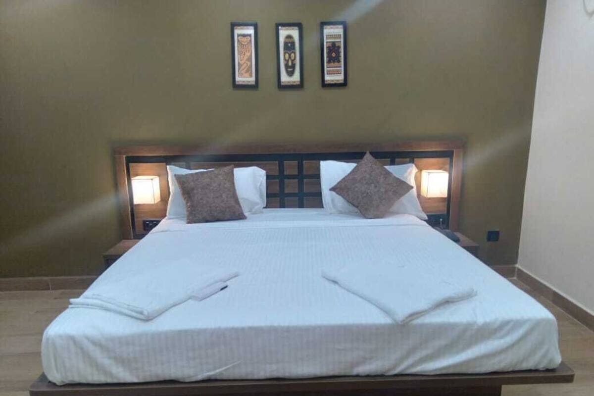 Cama com cabeceira de madeira, roupa de cama branca e duas luminárias de apoio.