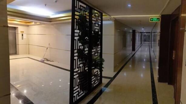 Corredor de hotel com design moderno, destacando um painel decorativo preto, pisos de mármore polido e um longo corredor que dá acesso a vários quartos.