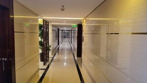 Corredor de hotel com piso lustroso, um caminho central e uma porta à esquerda.