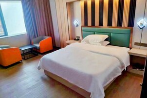 Quarto de hotel com uma cama grande, uma escrivaninha com cadeira e uma janela com cortinas.