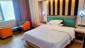 Quarto de hotel com uma cama grande, uma mesinha, uma cadeira laranja e uma mesa de cabeceira.