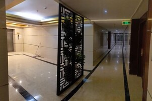 Corredor de hotel com painel decorativo preto, piso polido e sinalização de saída visível.