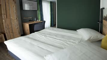 Quarto de hotel com uma cama grande, uma escrivaninha e uma televisão presa na parede.