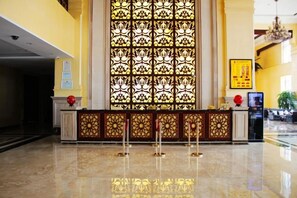 Um hall de hotel com uma mesa de recepção, uma ampla janela decorativa e um candelabro.