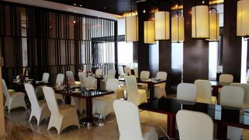 Um restaurante com várias mesas e cadeiras, luminárias de iluminação moderna e design de interiores contemporâneo.