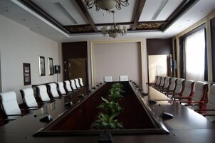 Uma sala de conferências com uma mesa comprida, cadeiras e um lustre.