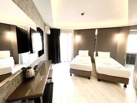 Quarto de hotel com cama, escrivaninha, televisão e janela.
