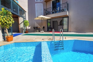 Piscina com escada, cercada por plantas em vasos e mobiliário de exterior.