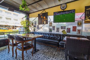 Um espaço de bar acolhedor com um sofá de couro preto, cadeiras de madeira e piso de azulejos.