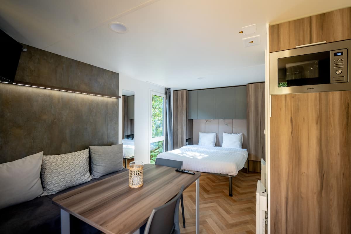Quarto de hotel moderno com cama, mesa de madeira, espaço de estar e micro-ondas embutido.