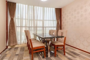 Sala de conferências com mesa de vidro, cadeiras bege, carpete estampado e grandes janelas com cortinas translúcidas.