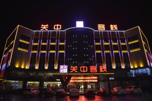Um edifício com letreiros iluminados e estacionamento com carros.
