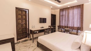Quarto de hotel com uma cama grande, uma escrivaninha com cadeira, televisão e ventoinha no teto.