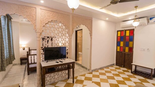 Quarto de hotel com piso xadrez, uma televisão sobre suporte de madeira, ventilador de teto e um painel decorativo na parede.