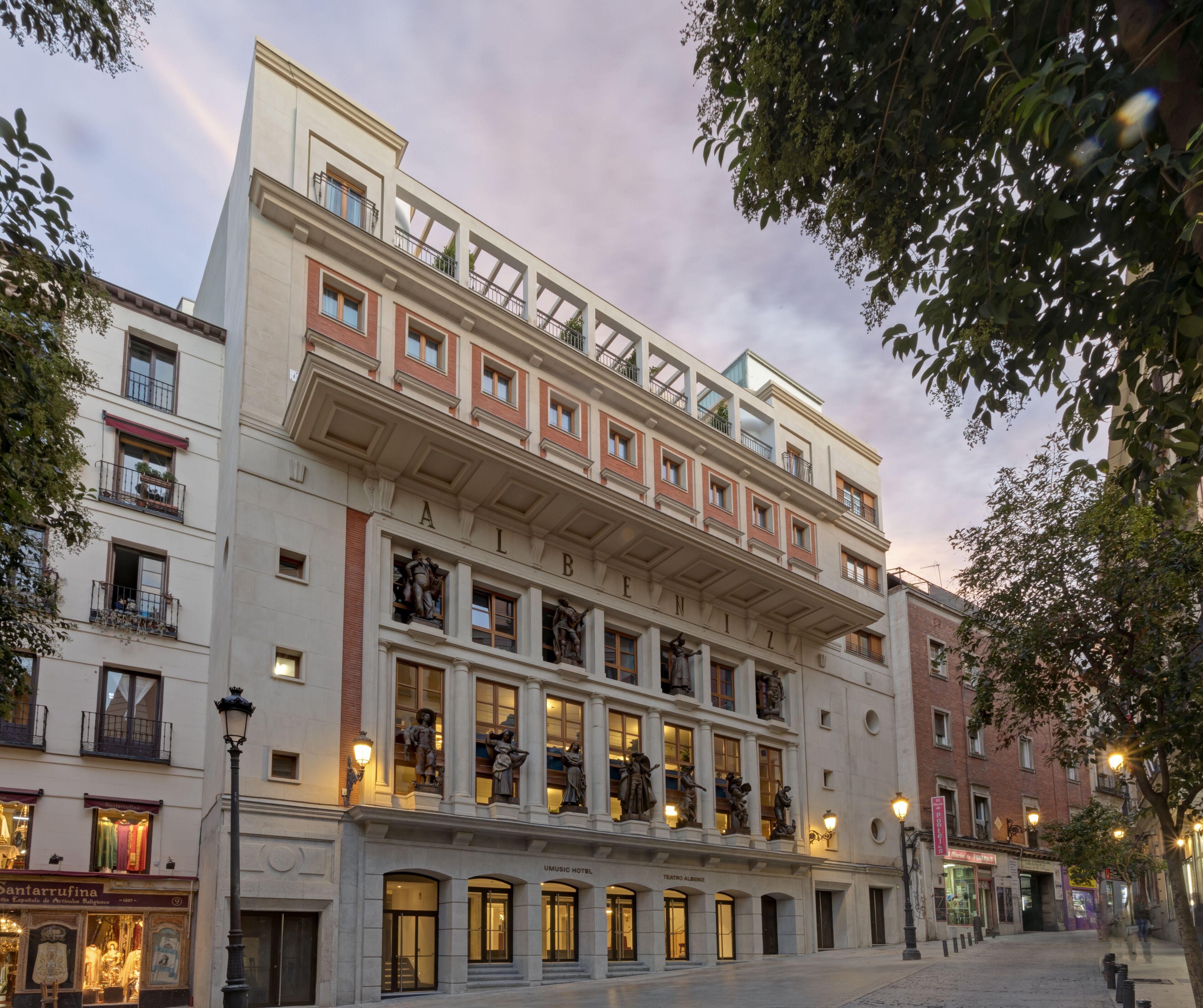 Um hotel com vários andares e fachada clássica, com entrada central, uma escadaria imponente, várias varandas e uma fileira de janelas com estátuas.