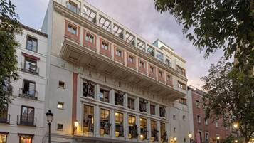 Um hotel com vários andares e fachada clássica, com entrada central, uma escadaria imponente, várias varandas e uma fileira de janelas com estátuas.