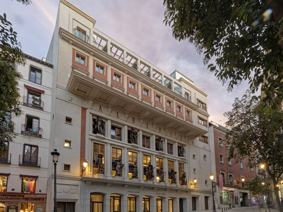 Um hotel com vários andares e fachada clássica, com entrada central, uma escadaria imponente, várias varandas e uma fileira de janelas com estátuas.